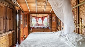 Quarto de cabana de madeira com cama, cortinas e janela com almofadas cor-de-rosa.