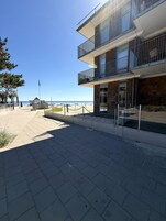 Um edifício moderno com varanda, vista para a praia e um calçadão.