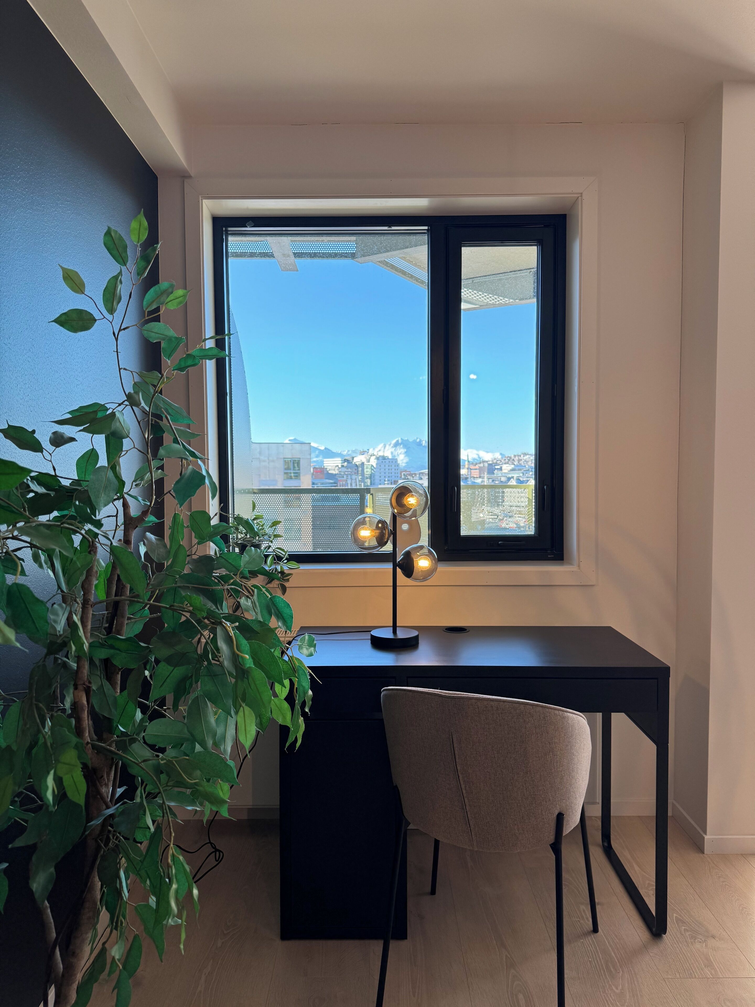 Quarto moderno com escrivaninha, cadeira e uma grande janela com vista para a cidade.