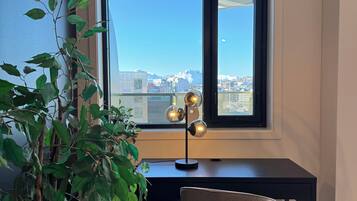 Quarto moderno com escrivaninha, cadeira e uma grande janela com vista para a cidade.