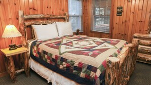 Quarto de cabana de madeira com cama, mesa de cabeceira e abajur.