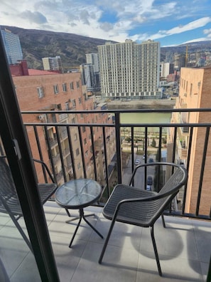 Varanda com duas cadeiras e uma mesa pequena, com vista para um horizonte urbano com diversos edifícios e uma montanha ao longe.
