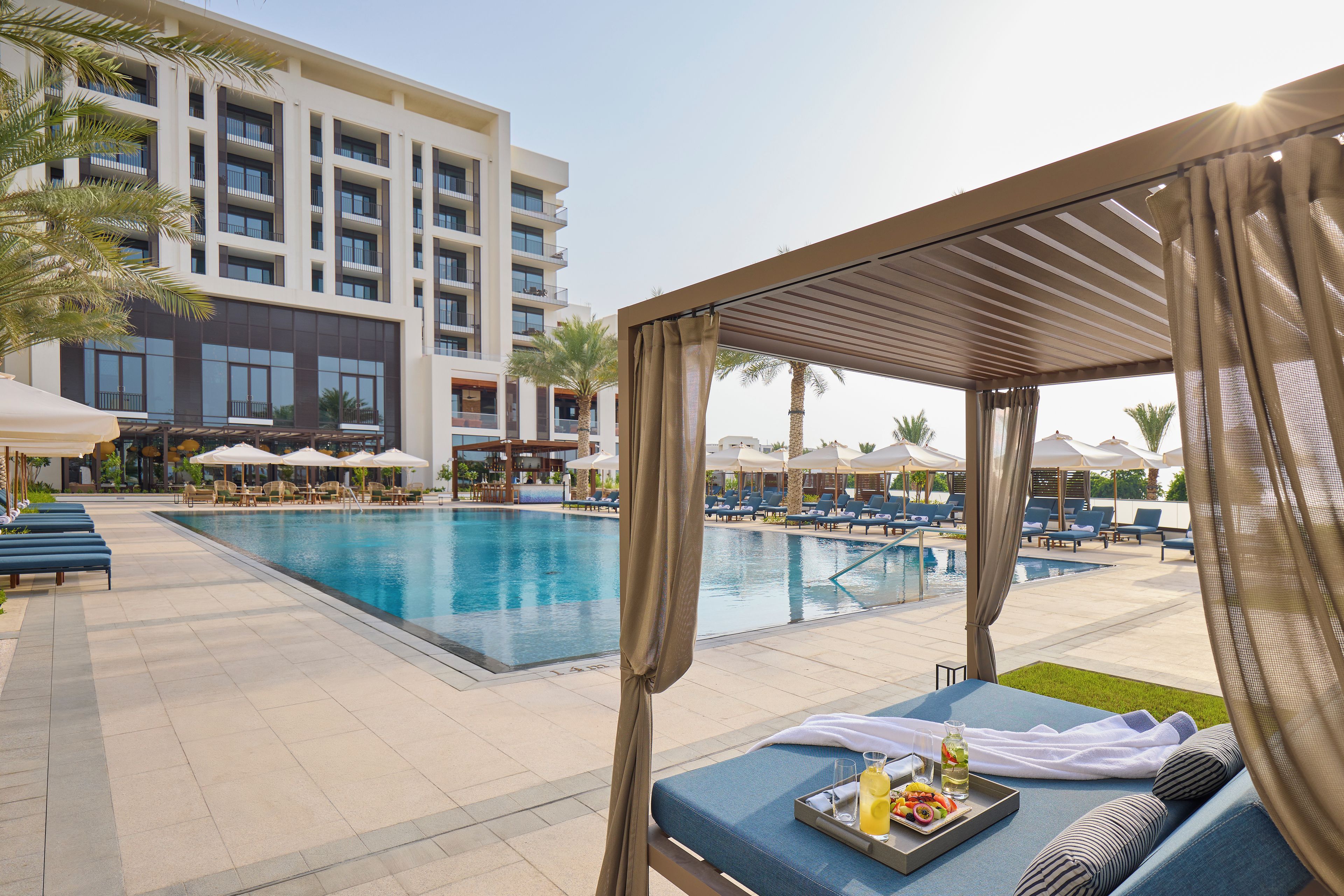Uma área à beira da piscina com espreguiçadeiras, um espaço de estar coberto e um edifício ao fundo.
