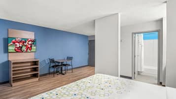 Quarto de hotel com cama, televisão na parede, secretária com cadeiras e zona de duche.