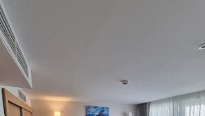 Quarto de hotel com cama, mesa de cabeceira, escrivaninha, cadeira, guarda-roupa e janela com cortinas.