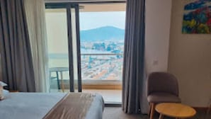 Quarto de hotel com cama, uma cadeira, uma mesinha e vista para a cidade pela janela.
