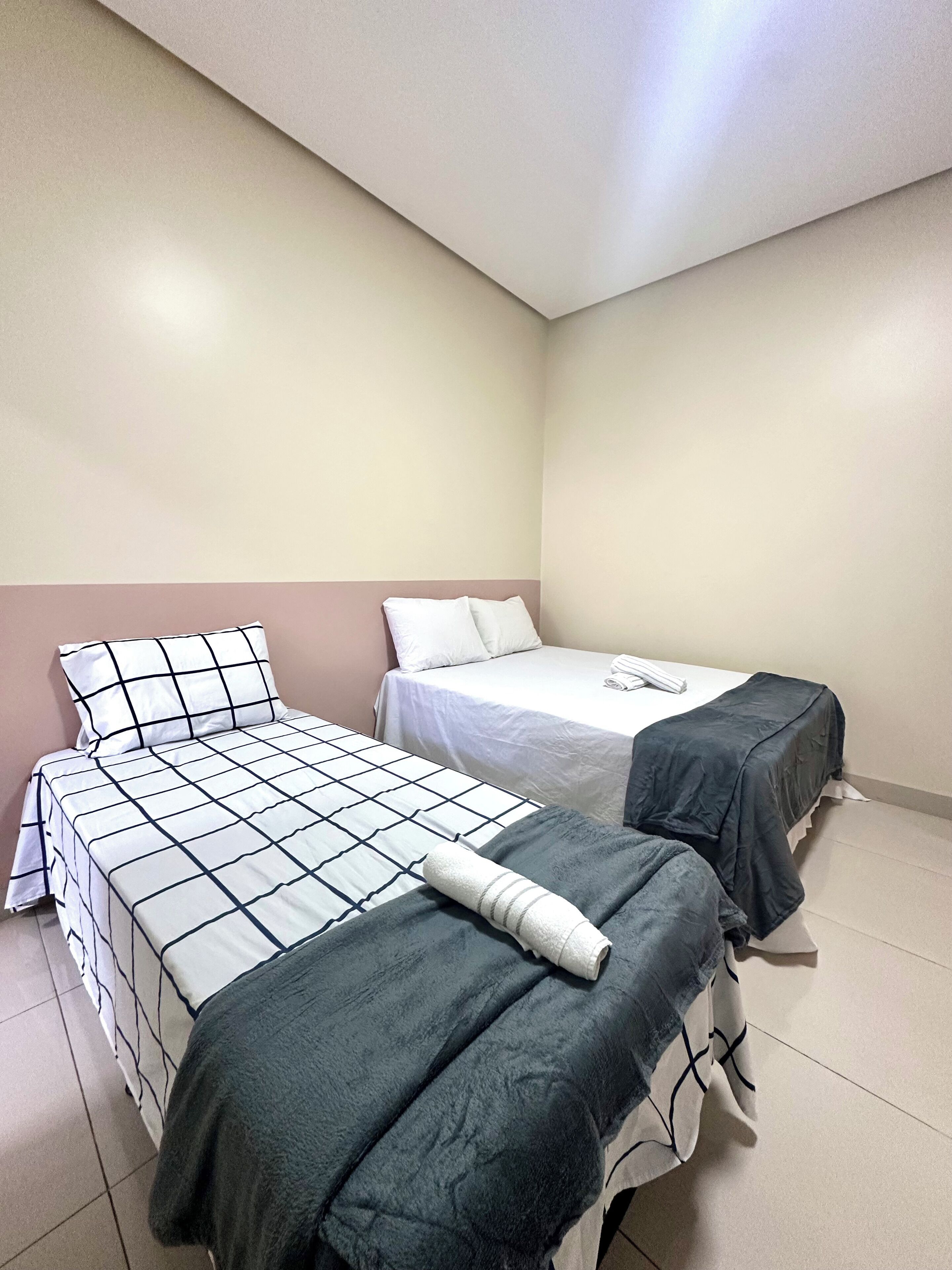 Quarto com duas camas, uma com colcha xadrez e outra com colcha branca lisa.