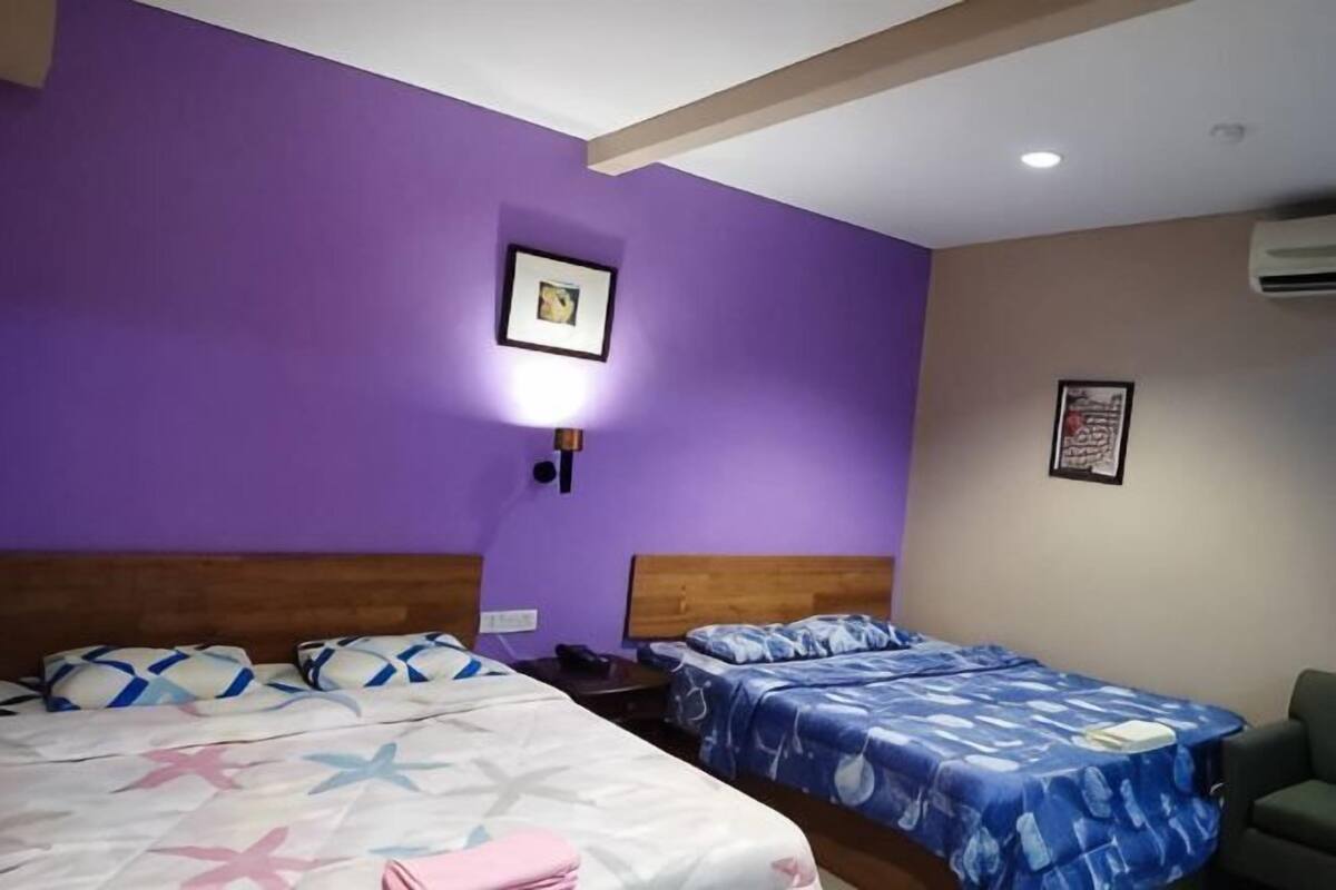 Quarto de hotel com duas camas, paredes roxas e um quadro pendurado na parede.