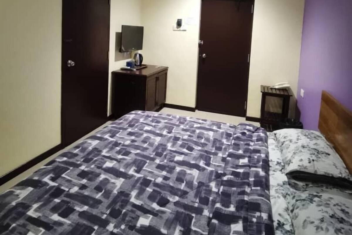 Quarto com cama, ventoinha no teto, mesa de cabeceira, uma pequena mesa e duas portas.