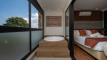 Quarto moderno com uma janela grande, uma banheira embutida e uma cama com manta listrada.