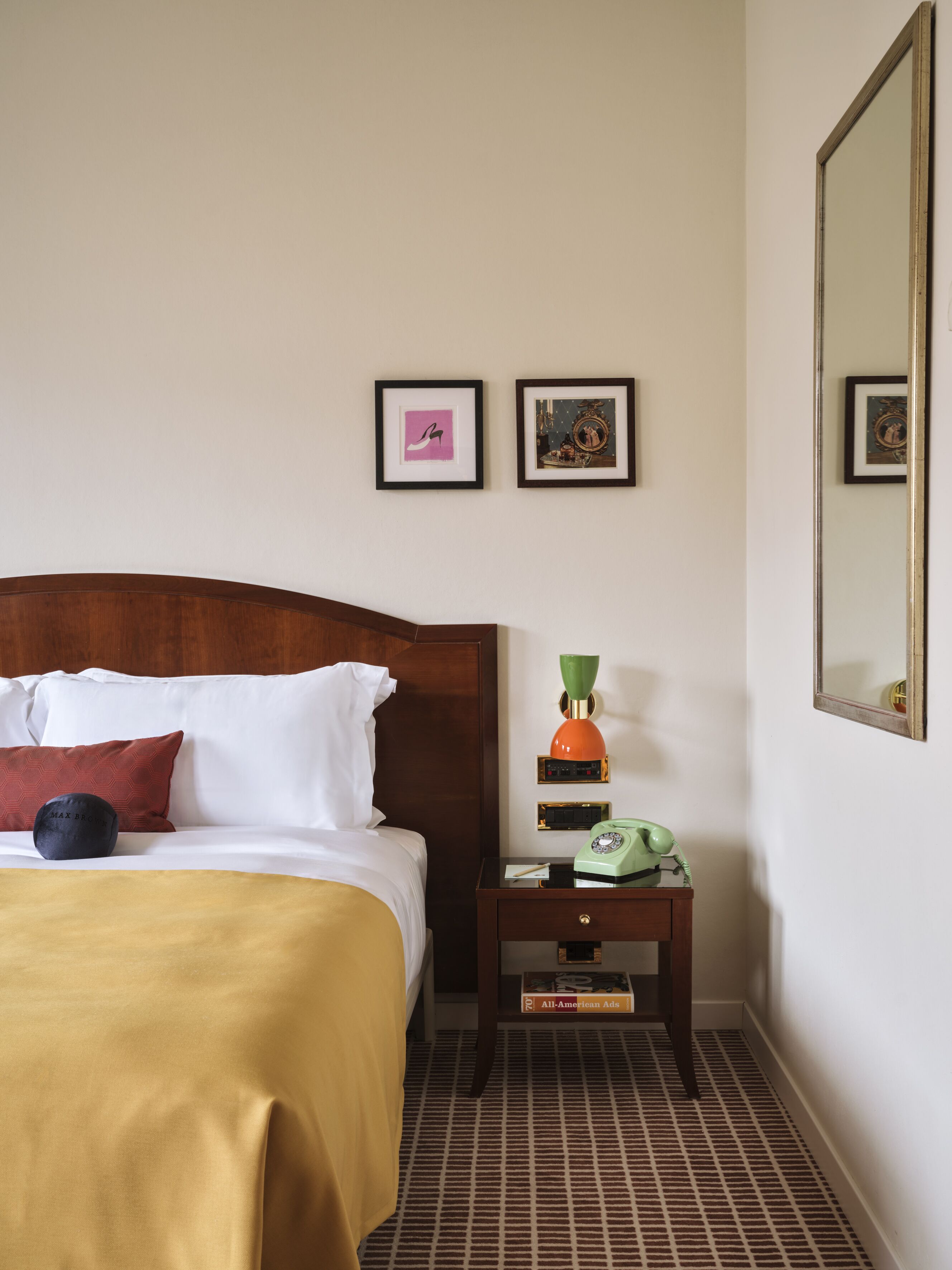 Quarto de hotel com cama, mesa de cabeceira com luminária, quadro emoldurado e espelho na parede.