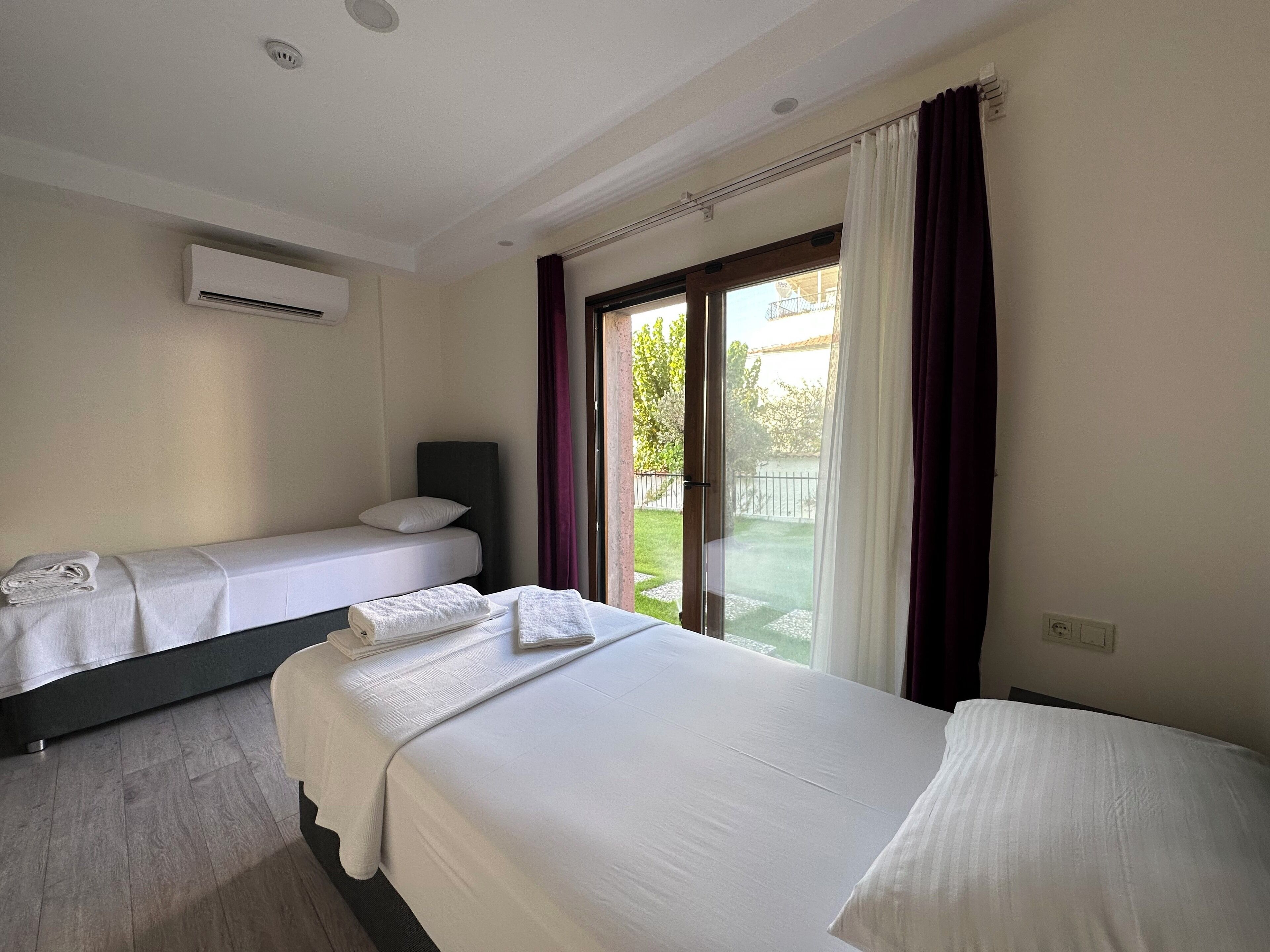 Quarto de hotel com duas camas, uma janela com cortinas e um aparelho de ar condicionado na parede.