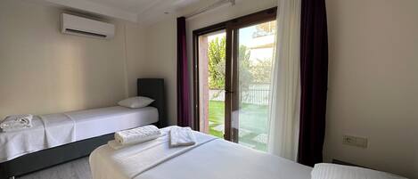 Quarto de hotel com duas camas, uma janela com cortinas e um aparelho de ar condicionado na parede.