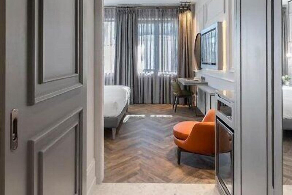 Quarto de hotel com cama, escrivaninha, cadeira e televisão.