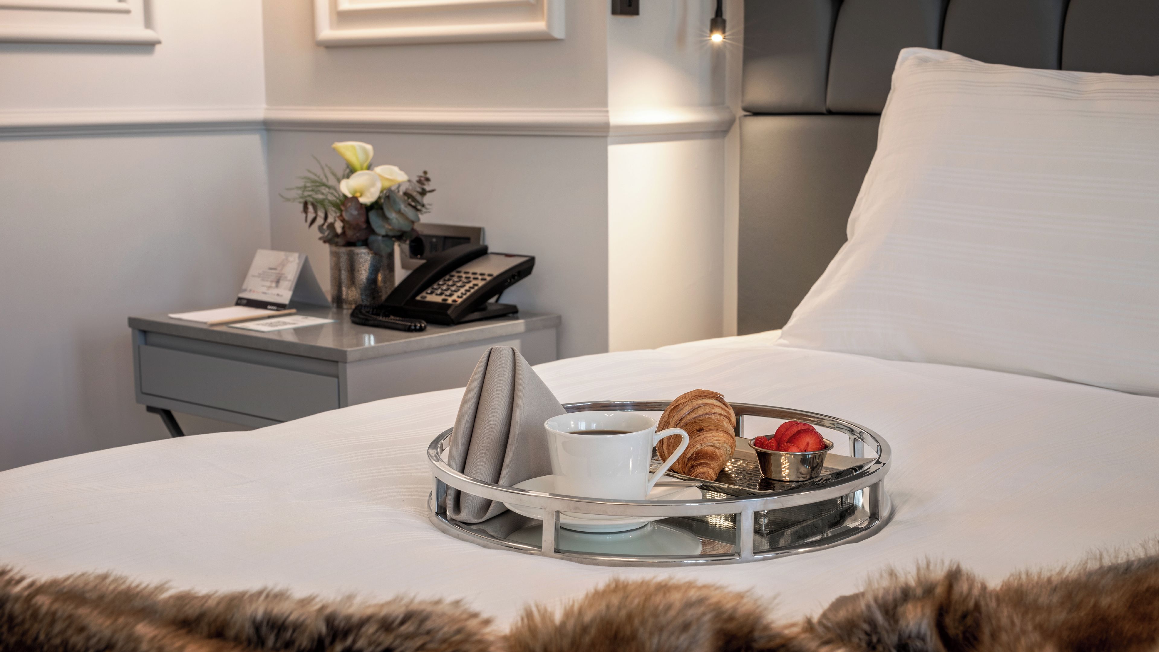 Cama bem arrumada com uma bandeja de itens de café da manhã, incluindo croissants, morangos e uma xícara de café.