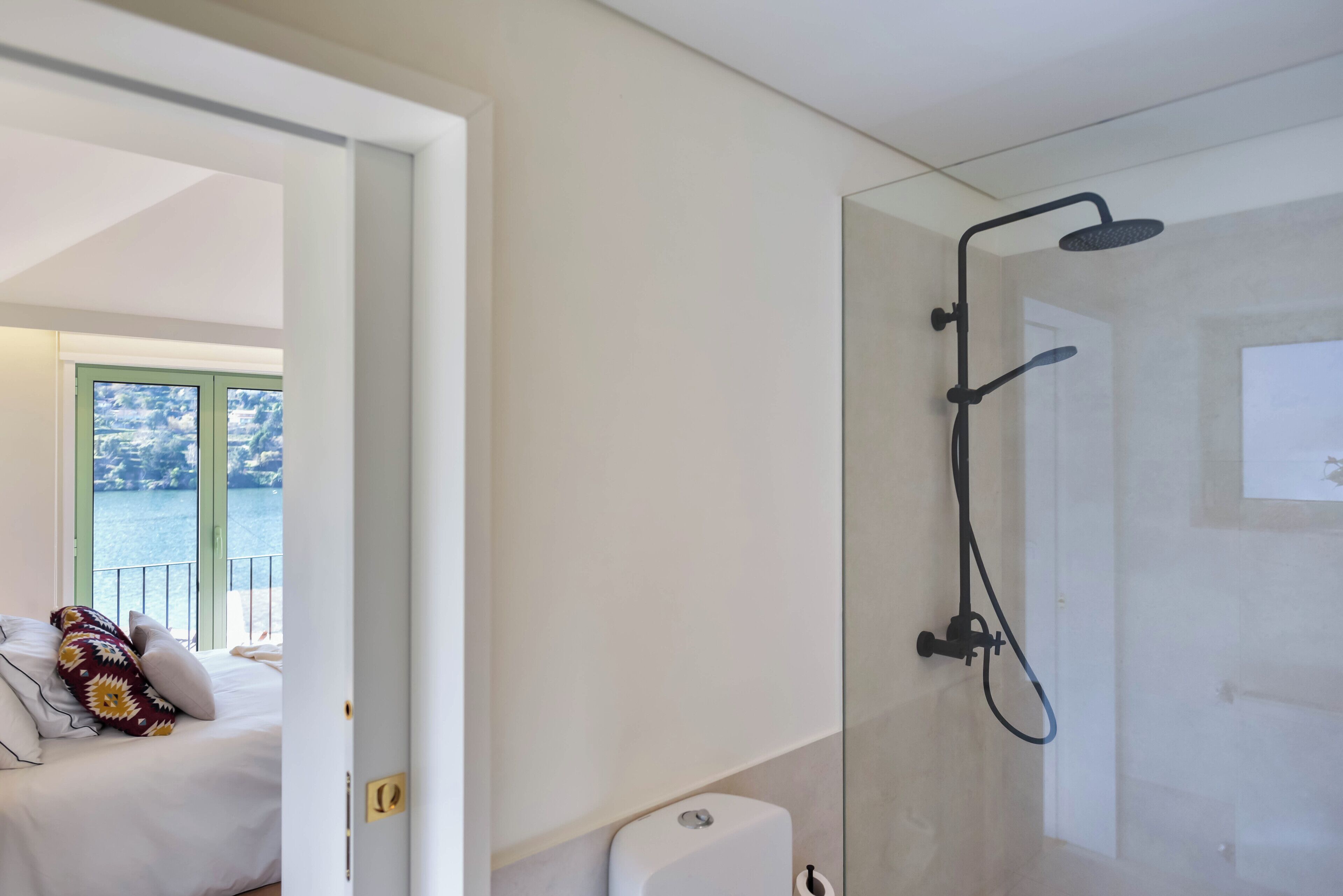 Uma casa de banho moderna com chuveiro envidraçado, sanita e cama com almofadas.