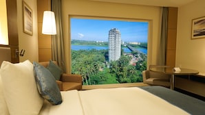 Quarto de hotel com uma cama grande, vista para um prédio alto, uma mesa de jantar e uma cadeira.