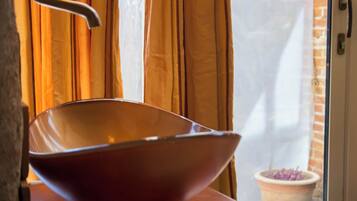 Uma tigela vermelha sobre uma superfície de madeira, cortinas, uma janela e uma porta.