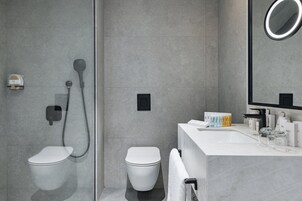 Uma casa de banho moderna com chuveiro em cabine de vidro, sanita branca e toucador com espelho e produtos de higiene pessoal.