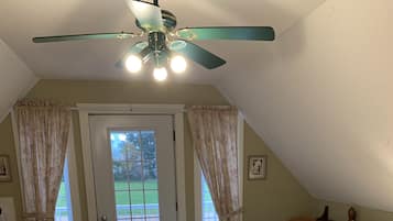 Quarto com duas camas, cabeceiras de madeira, ventilador de teto e vista para um gramado verde através de uma porta.