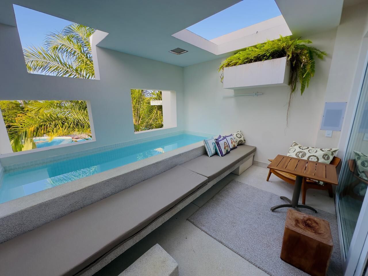 Uma área interna de piscina moderna com vista desobstruída para o exterior, um espaço de estar com uma mesa e um banquinho de madeira.