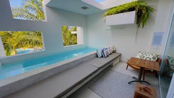 Uma área interna de piscina moderna com vista desobstruída para o exterior, um espaço de estar com uma mesa e um banquinho de madeira.