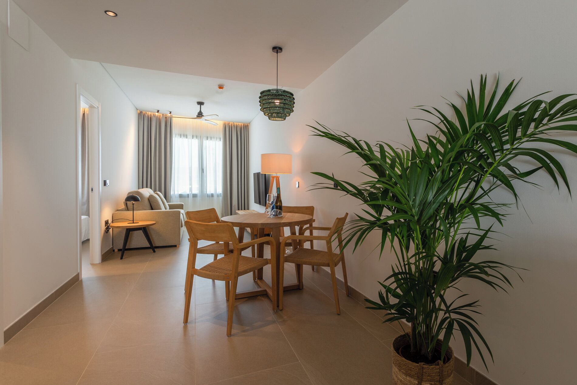 Uma sala de estar moderna com um sofá, uma mesa de jantar com cadeiras, um abajur e uma grande planta em vaso.