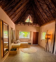 Quarto com telhado de palha, cama com vista, pintura em suporte e janela com cortinas.