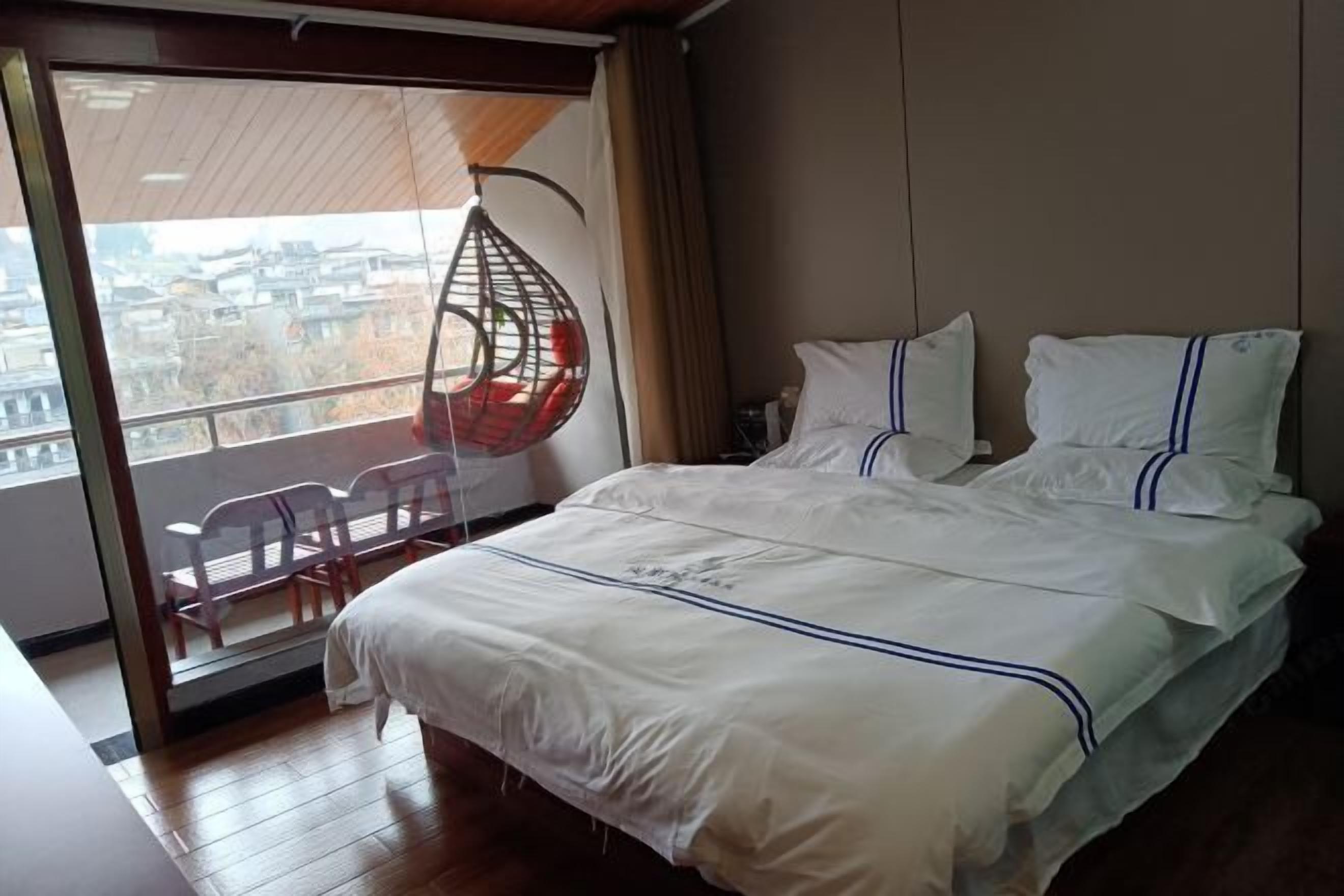 Quarto de hotel com uma cama grande, uma cadeira suspensa perto da janela e vista para o horizonte urbano.