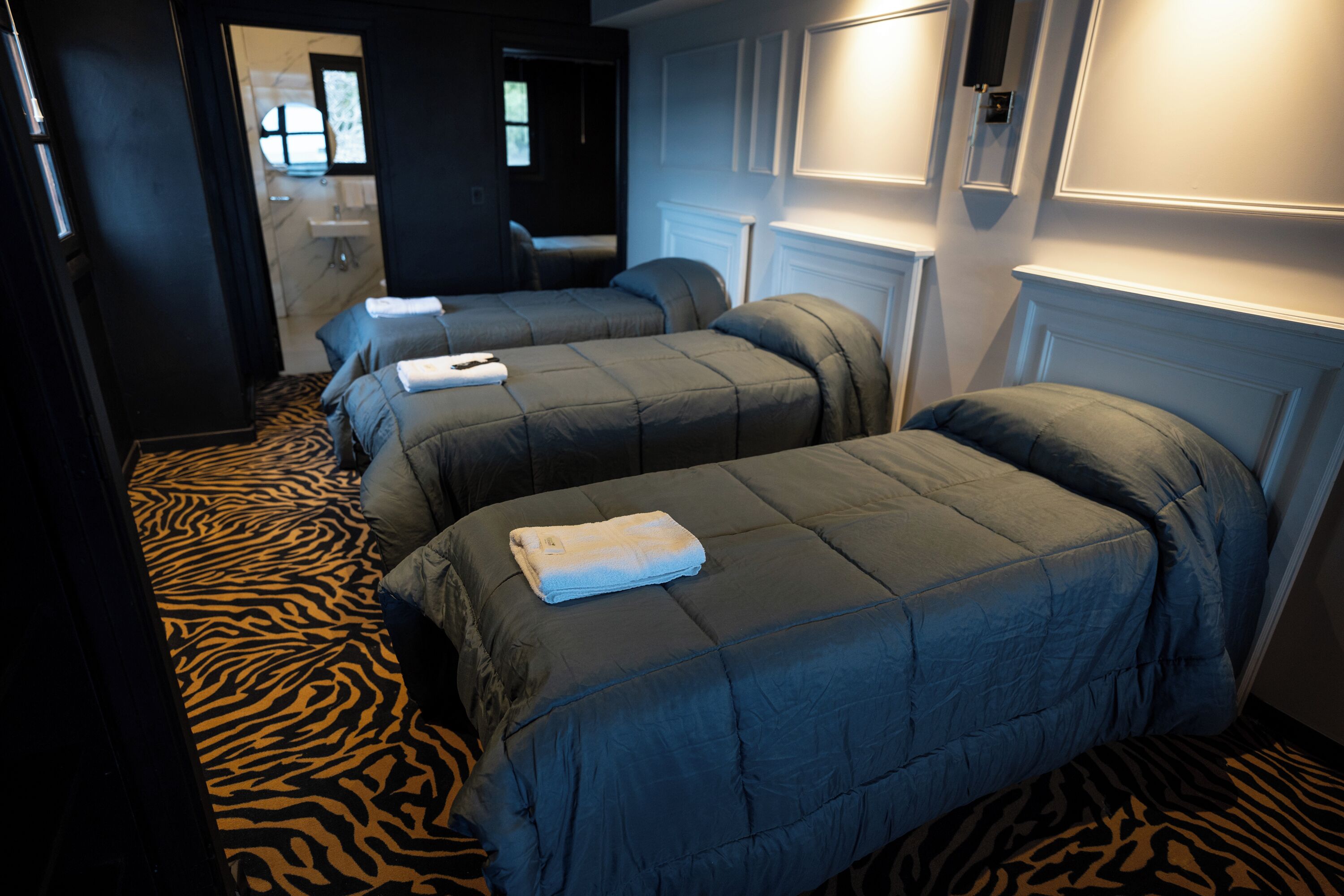 Quarto de hotel com três camas, carpete com padrão de zebra e vista para o banheiro.