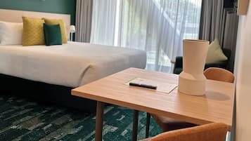 Quarto de hotel com uma cama, uma mesa com controle remoto, uma cadeira e uma televisão presa na parede.