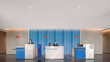 Uma área de recepção de hotel com três balcões, cada um com um computador e uma luminária vermelha.