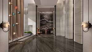 Um corredor moderno com piso de mármore escuro, painéis verticais de madeira e arandelas decorativas.