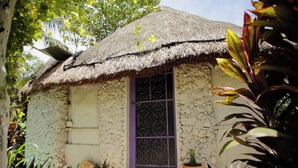 Uma casa rústica com telhado de palha, uma porta roxa e um vaso de planta em frente.