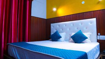 Quarto de hotel com uma cama grande, cortinas vermelhas, cabeceira branca e uma parede amarela.