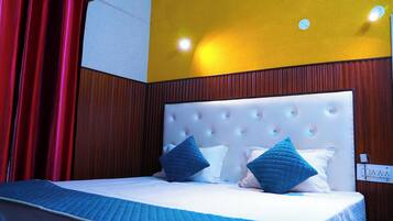 Quarto de hotel com cabeceira estofada, cama com roupa de cama branca e azul, e cortinas vermelhas.