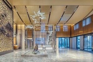 Um hall espaçoso com design moderno, com balcão de recepção, uma grande escultura e teto alto com iluminação embutida.