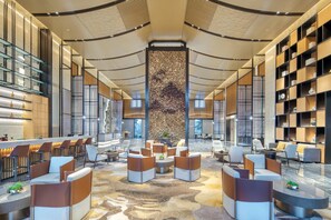 Um lobby espaçoso com assentos modernos, uma parede decorativa central e um espaço de bar.