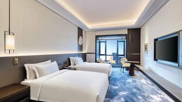 Quarto de hotel com duas camas, uma escrivaninha, uma cadeira, uma televisão e uma janela grande com vista.