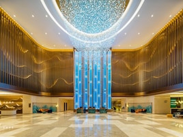 Um hall amplo com teto alto, uma coluna central iluminada em azul e um balcão de recepção.