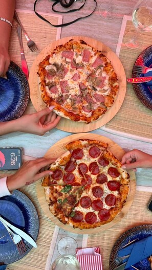Duas pizzas sobre tábuas de madeira, um smartphone e um copo de água em uma mesa.