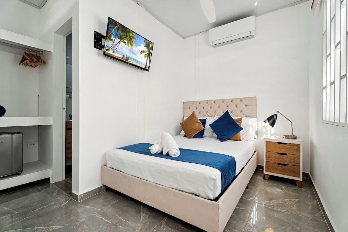 Um quarto moderno com uma cama, televisão na parede, guarda-roupa, mesa de cabeceira e ar condicionado.