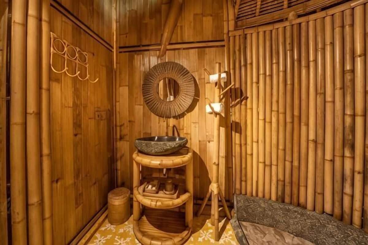 Quarto de madeira com um espelho circular, um prateleira com sapatos e um pequeno banquinho.