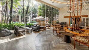 Amplo espaço interno com piso de madeira curvo, móveis de vime e grandes janelas com vista para palmeiras e uma piscina.