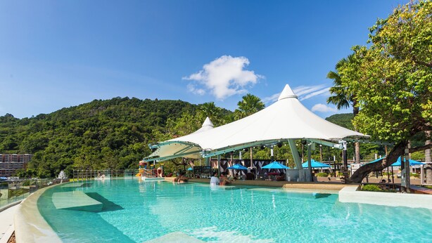 Piscina cristalina com estrutura de toldo branco, rodeada por vegetação exuberante e uma paisagem montanhosa.