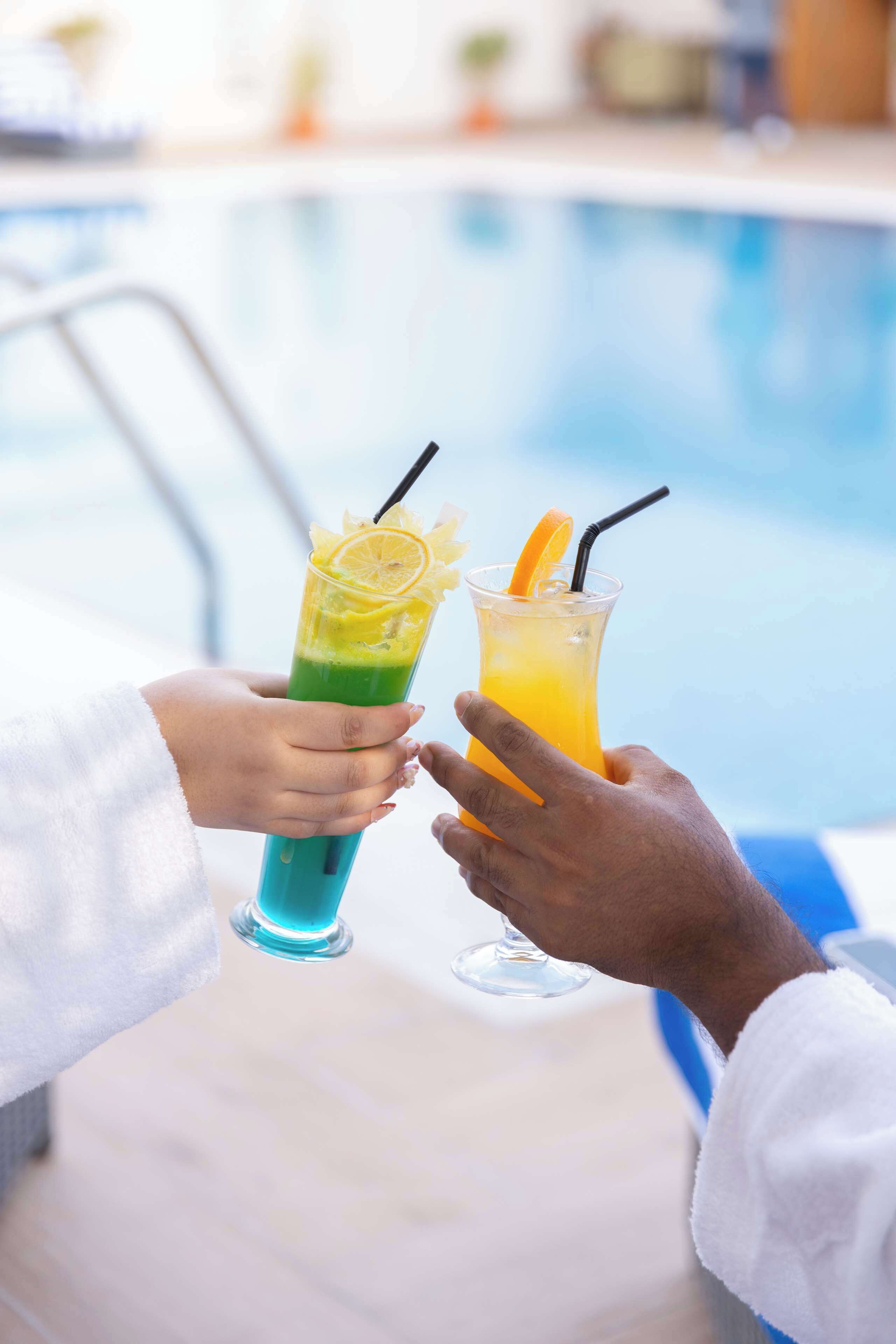 Duas pessoas segurando copos com bebidas à beira da piscina.