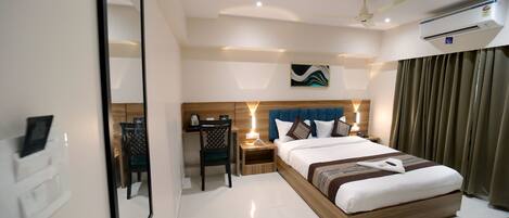 Quarto de hotel moderno com uma cama grande, uma escrivaninha, uma cadeira, um criado-mudo, um espelho e um aparelho de ar condicionado.