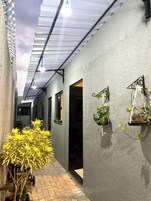 Uma passagem estreita com telhado de metal corrugado, plantas em vasos e um caminho de tijolos.