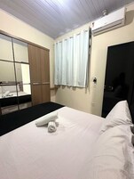 Quarto de hotel com cama, guarda-roupa, espelho, janela com cortinas e unidade de ar condicionado.