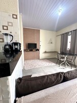 Uma sala de estar moderna com televisão de tela plana, cafeteira e área de jantar com mesa e cadeiras.